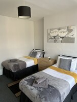 Quarto de hotel com duas camas, uma mesa de cabeceira, um abajur e um quadro na parede.