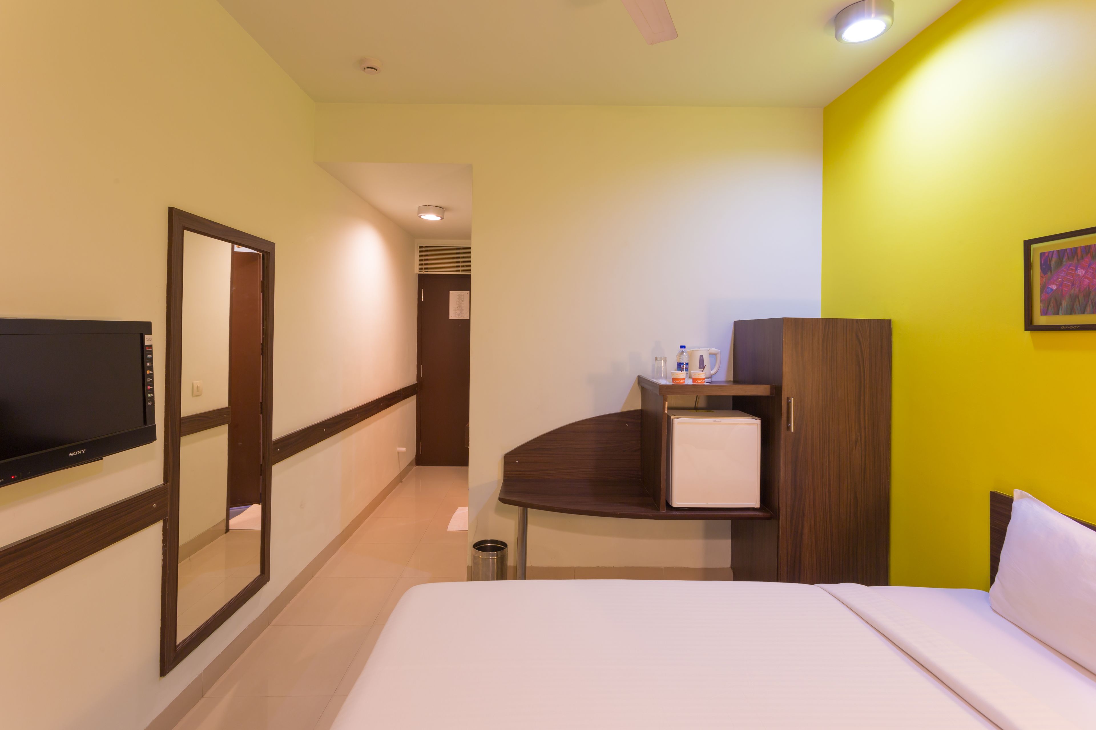 Quarto de hotel com cama, televisão, secretária com computador e pequeno armário.