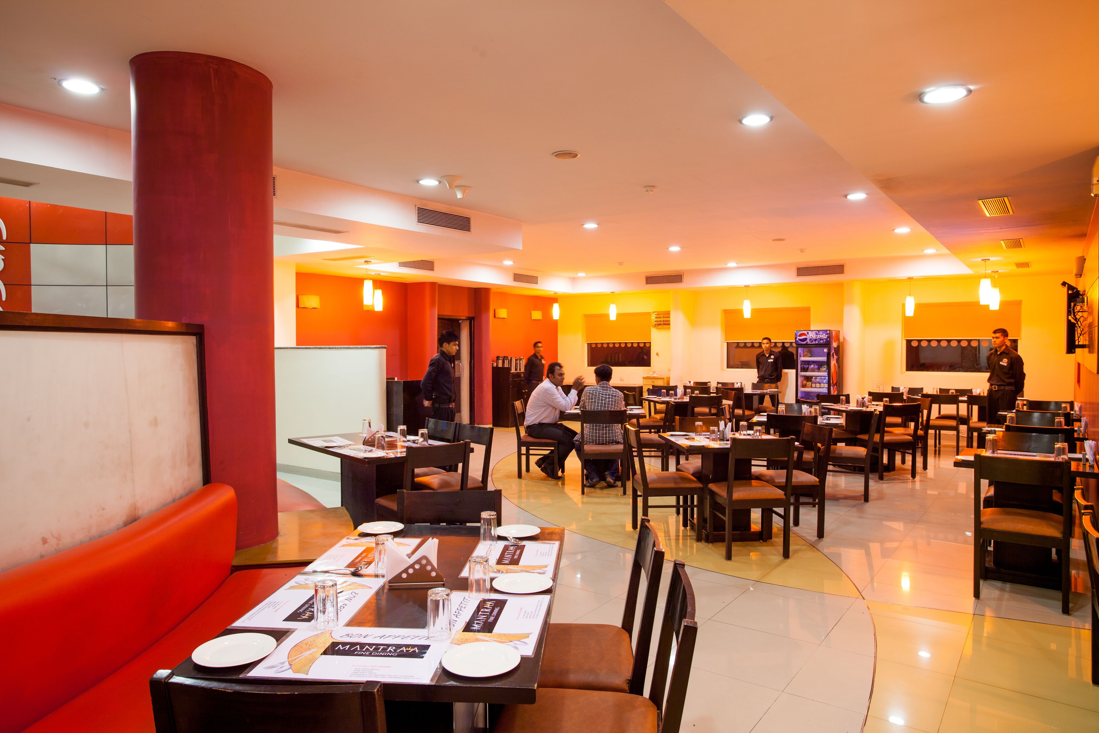 Restaurante com várias mesas e cabines, um pilar vermelho e decoração luminosa.