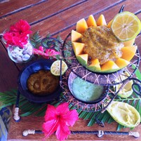 Disposição de mesa com tema tropical, salada de frutas, um recipiente com molho e flores decorativas.