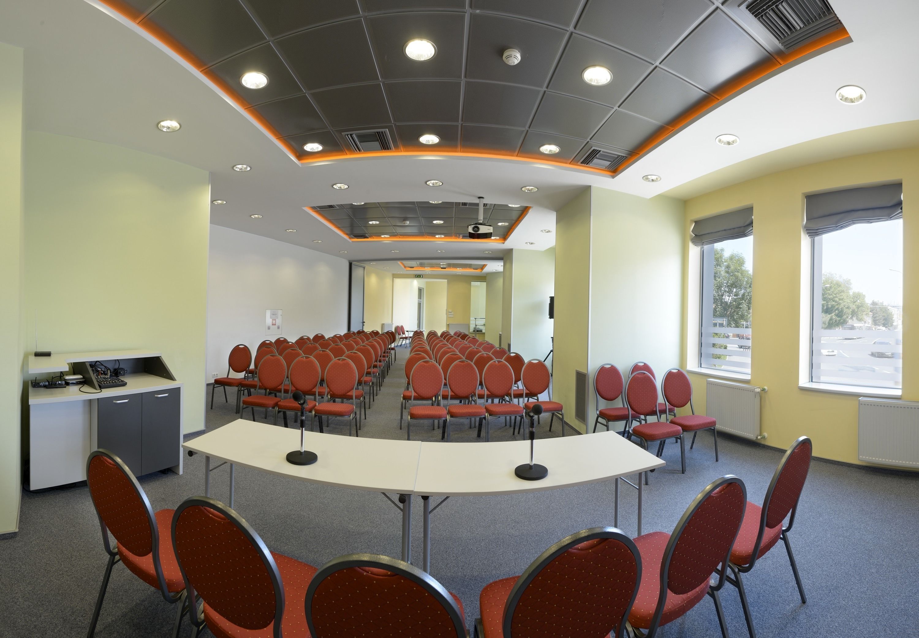 Uma sala de conferência com uma mesa grande, fileiras de cadeiras, um pódio e uma mesa com um telefone.