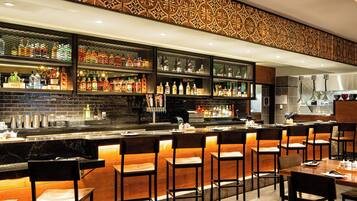 Uma área de bar com um balcão comprido, diversas garrafas de bebidas e banquetas.