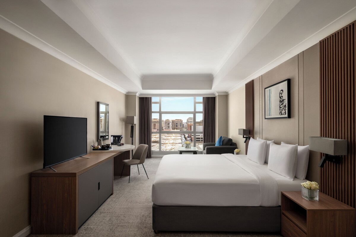 Quarto de hotel com uma cama grande, uma escrivaninha, uma televisão e vista para a cidade.