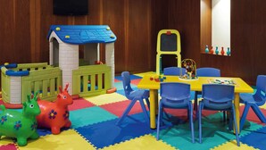 Um espaço de brincadeiras com casinha, tapetes coloridos e uma mesa com cadeiras.