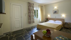 Um quarto com cama, janela com cortinas, mesa de cabeceira com abajur e uma tigela de frutas na mesa.