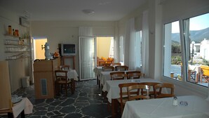 Uma área de refeições com mesas e cadeiras, um espaço de cozinha com geladeira, e vista para o exterior.