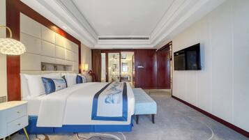 Quarto de hotel com uma cama grande, uma mesinha de cabeceira, televisão na parede e vista para o corredor.