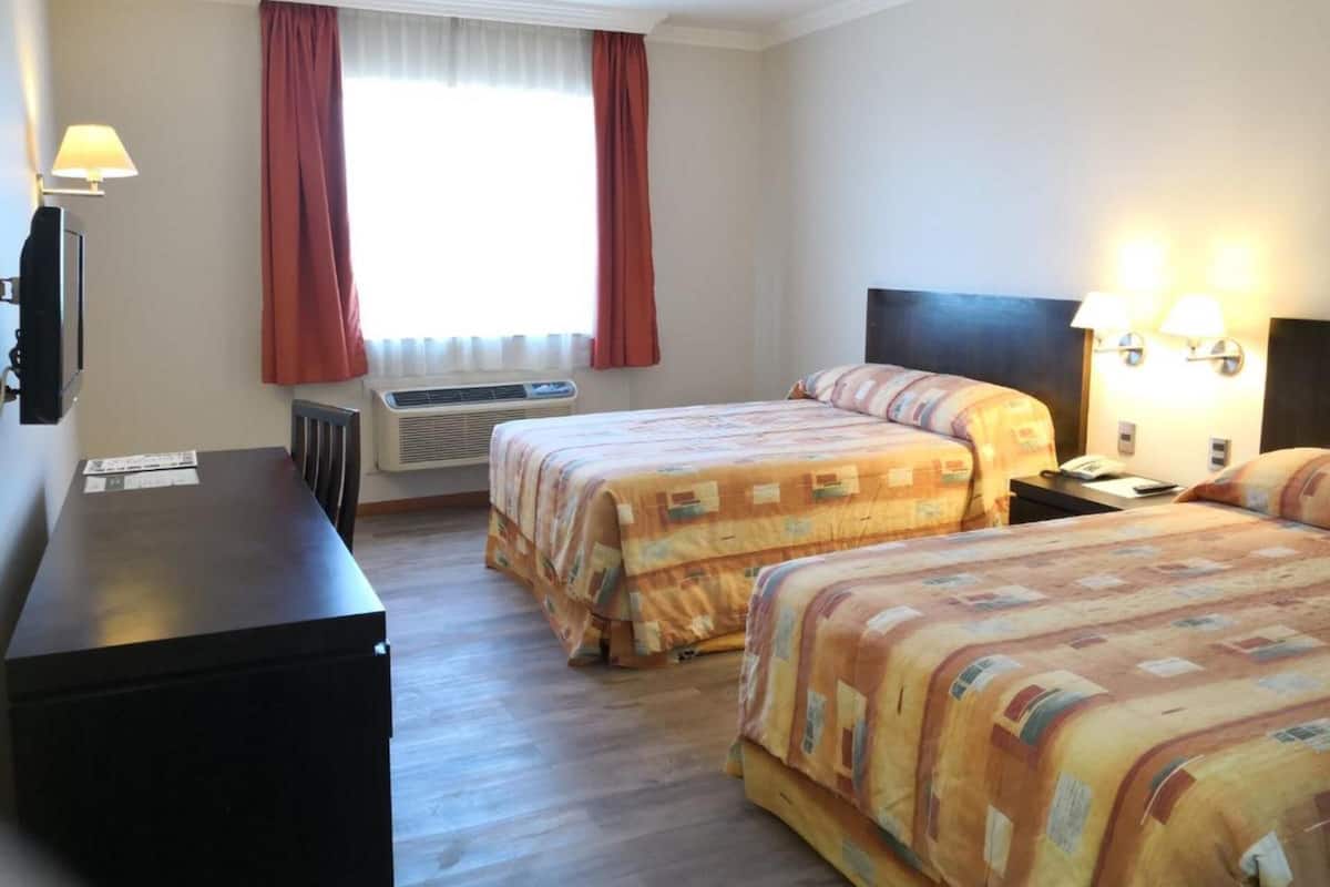 Quarto de hotel com duas camas, uma escrivaninha, uma televisão e uma janela com cortinas.