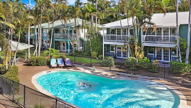 Piscina cercada por área com espreguiçadeiras e um prédio de dois andares com varandas.
