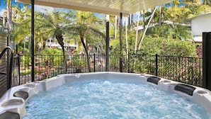 Uma banheira de hidromassagem com vista para um jardim tropical e um espaço de pátio coberto.
