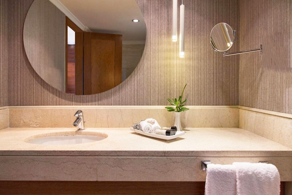 Uma casa de banho moderna com um espelho redondo, uma pia e uma pequena planta no lavatório.