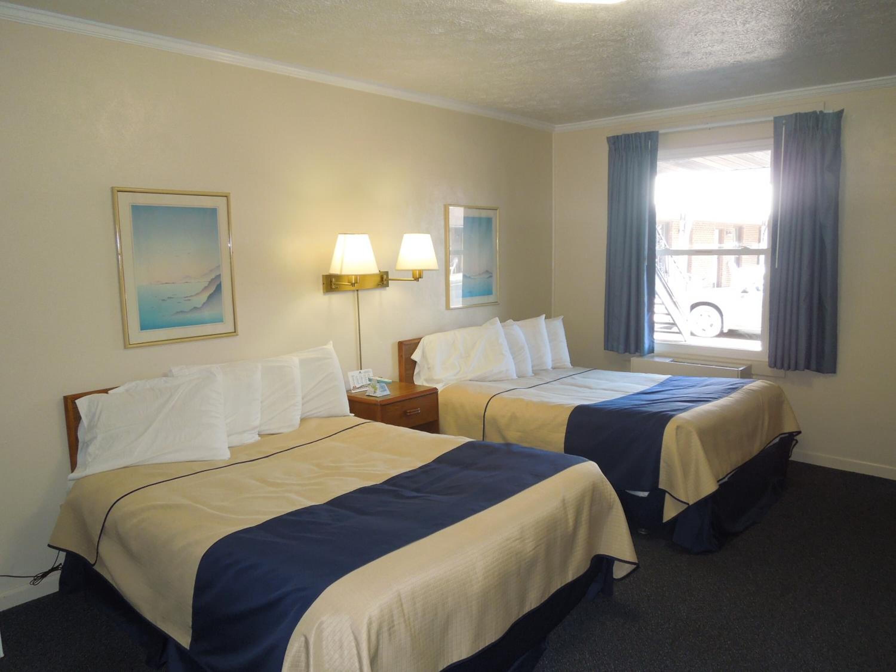 Quarto de hotel com duas camas, uma janela com cortinas e luminárias fixadas na parede.