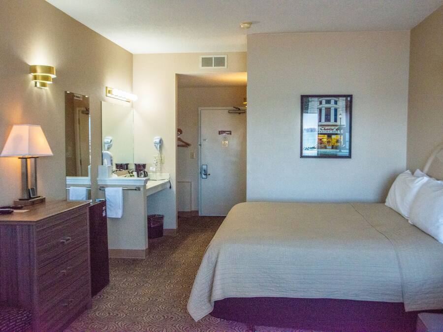 Quarto de hotel com cama, penteadeira, espelho e quadro na parede.