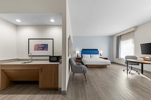 Quarto de hotel com cama, escrivaninha, cadeira, televisão e um quadro na parede.