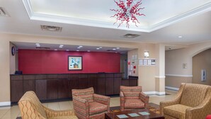 Um lobby com balcão de recepção, poltronas listradas, um sofá vermelho e um tapete estampado.