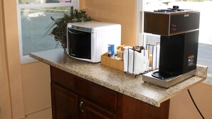 Cozinha com micro-ondas, máquina de café e um vaso de planta no balcão.
