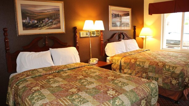 Quarto de hotel com duas camas, cada uma com roupa de cama estampada com flores, cabeceira de madeira, luminária de cabeceira e mesa de cabeceira com telefone.