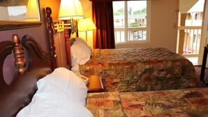 Quarto de hotel com cama, mesa de cabeceira com abajur, telefone e janela com vista para o exterior.