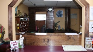 Uma área de recepção com um balcão de madeira, um relógio, um mural de avisos e uma placa com a inscrição 'Toque o Sino para Atendimento'.