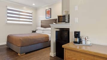 Quarto com cama, geladeira, micro-ondas e cafeteira sobre uma mesa de madeira.