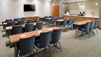 Uma sala de conferências com mesas, cadeiras, uma televisão, um espaço para café e uma porta.