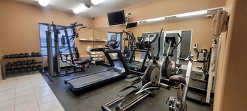 Uma academia com esteiras, aparelhos de musculação e halteres.