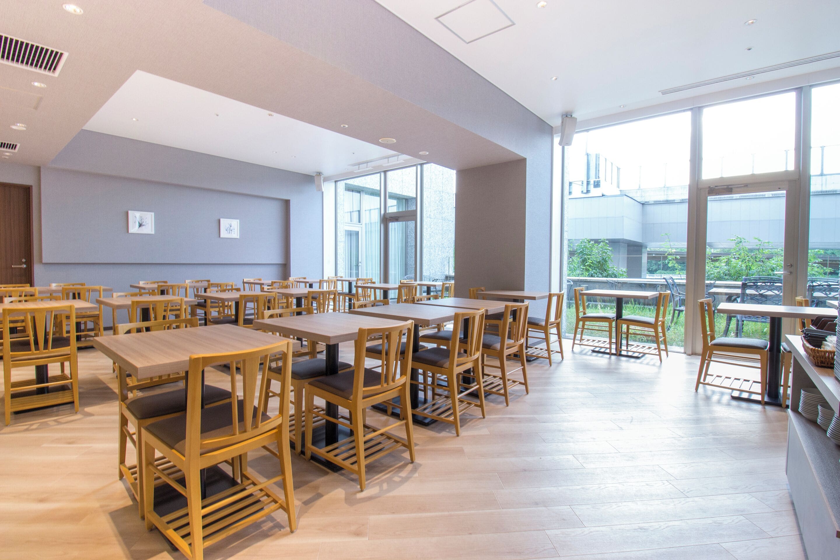 Uma sala de jantar espaçosa com mesas e cadeiras de madeira, amplas janelas com vista para o exterior e um design de teto moderno.