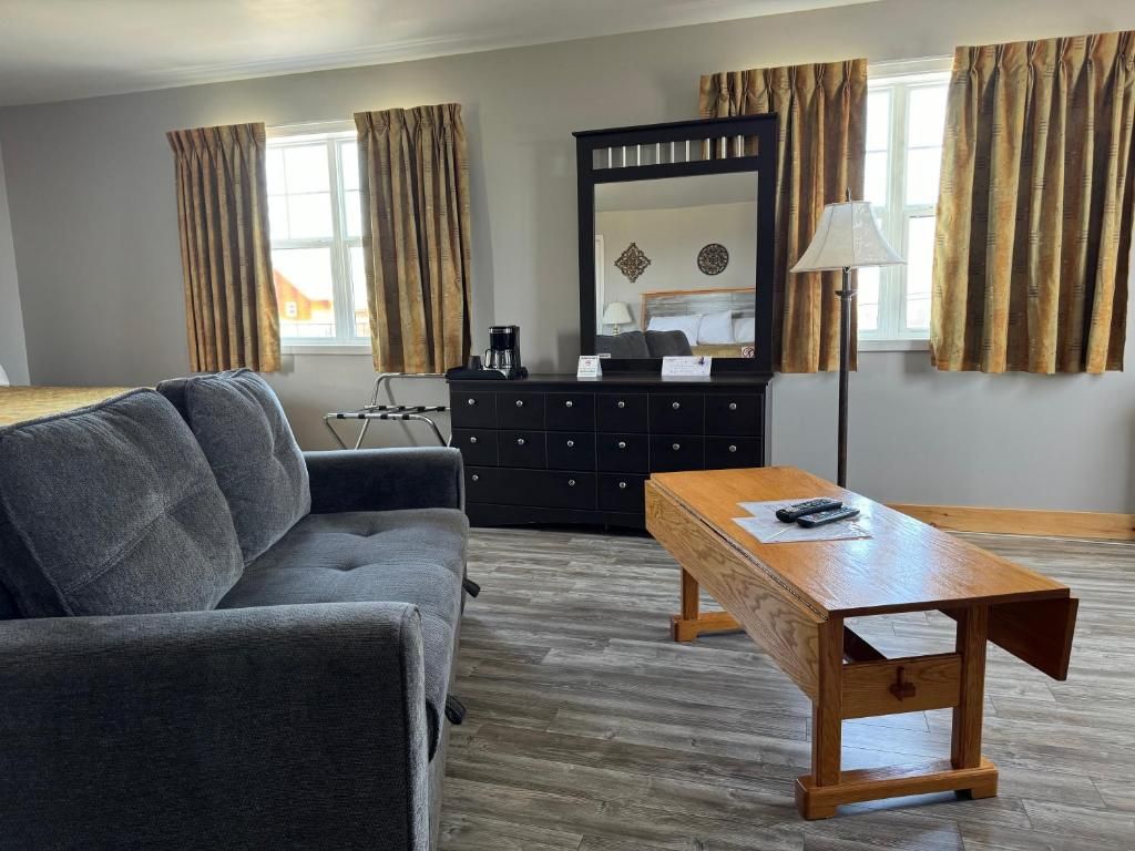 Quarto de hotel com sofá, mesa de centro de madeira, cômoda, espelho e cortinas.