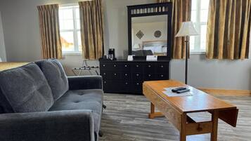 Quarto de hotel com sofá, mesa de centro de madeira, cômoda, espelho e cortinas.