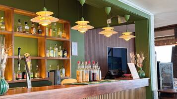 Uma área de bar com prateleiras de madeira repletas de garrafas de bebidas, balcão e luminárias pendentes.