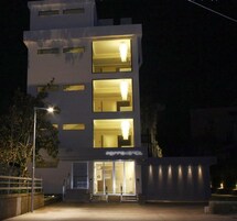 Um hotel moderno com fachada de vidro, vários andares e uma entrada bem iluminada.