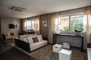 Uma sala de estar moderna com um conjunto de sofá, uma televisão de tela plana na parede e uma grande janela com cortinas.