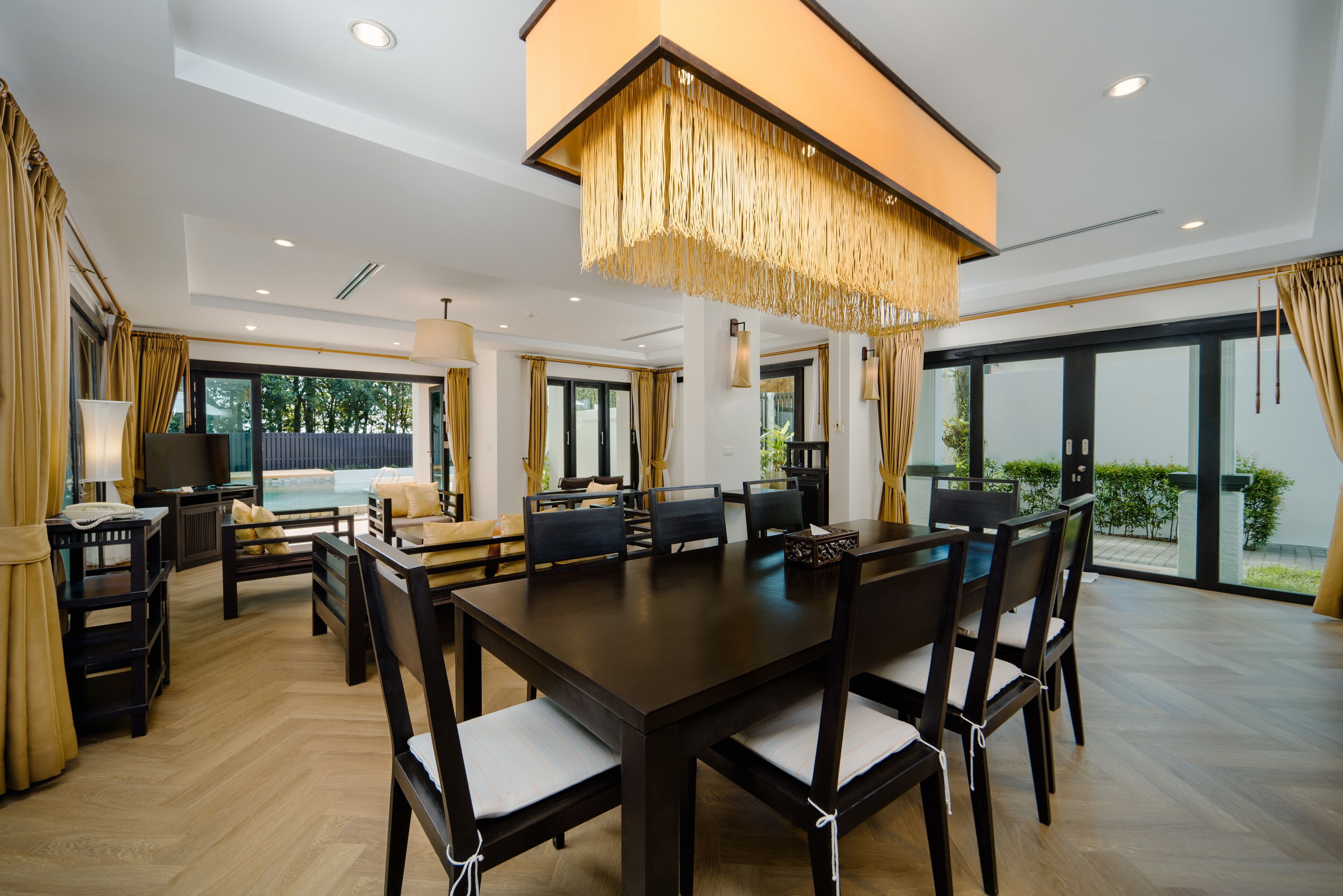 Uma sala de jantar espaçosa com uma grande mesa de madeira e cadeiras, um lustre pendurado e janelas amplas com vista para o exterior.