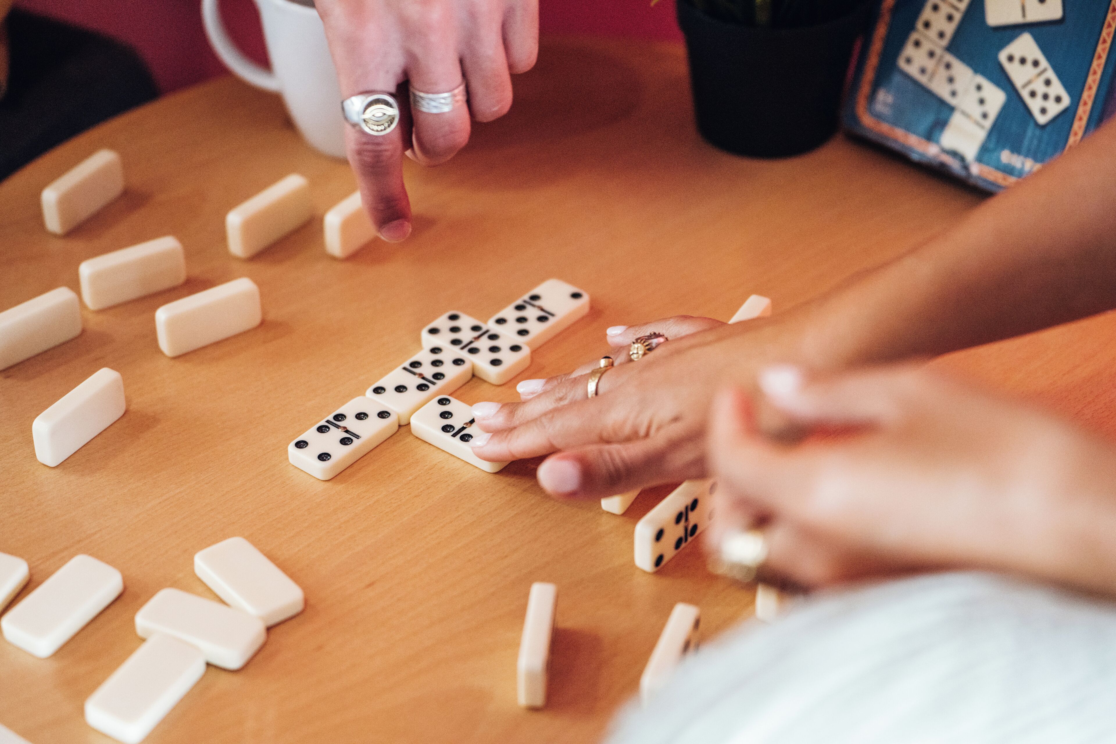Close-up de mãos jogando dominó em uma mesa de madeira.