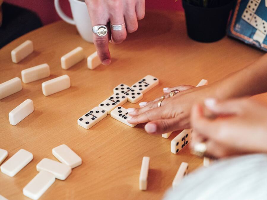 Close-up de mãos jogando dominó em uma mesa de madeira.