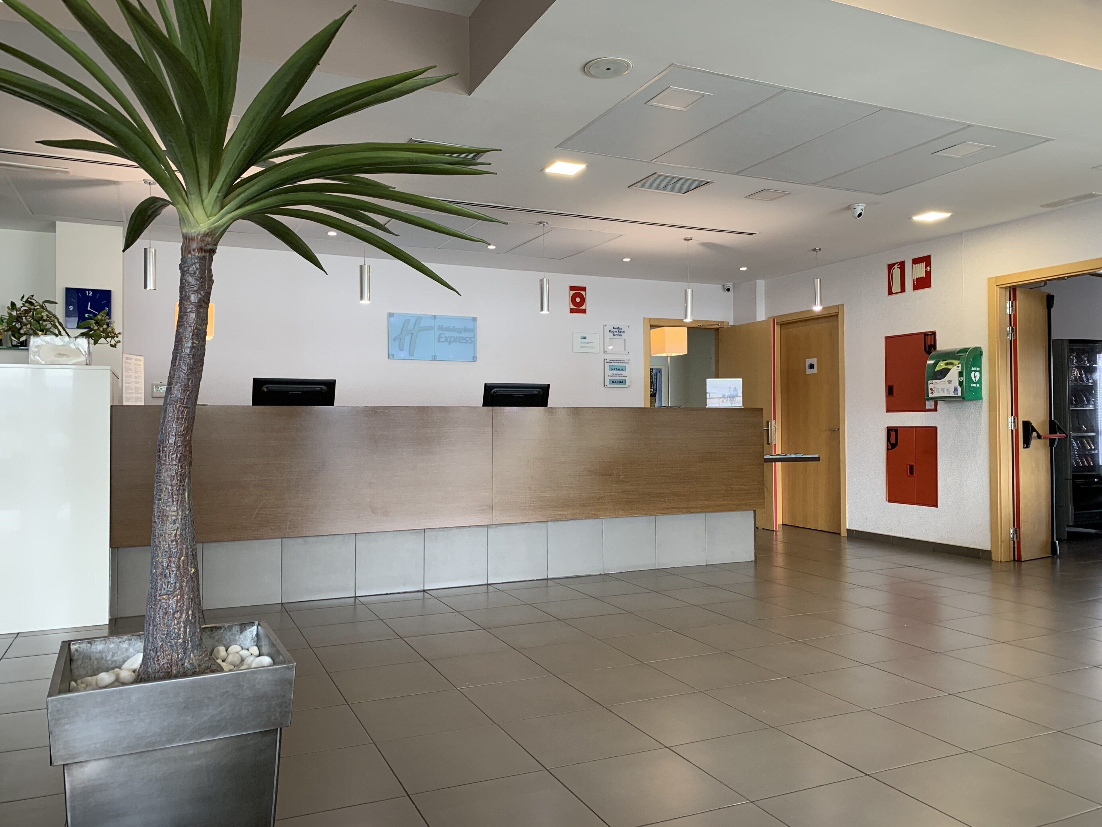 Bancada de recepção com uma planta, um relógio e uma placa indicando um hotel.