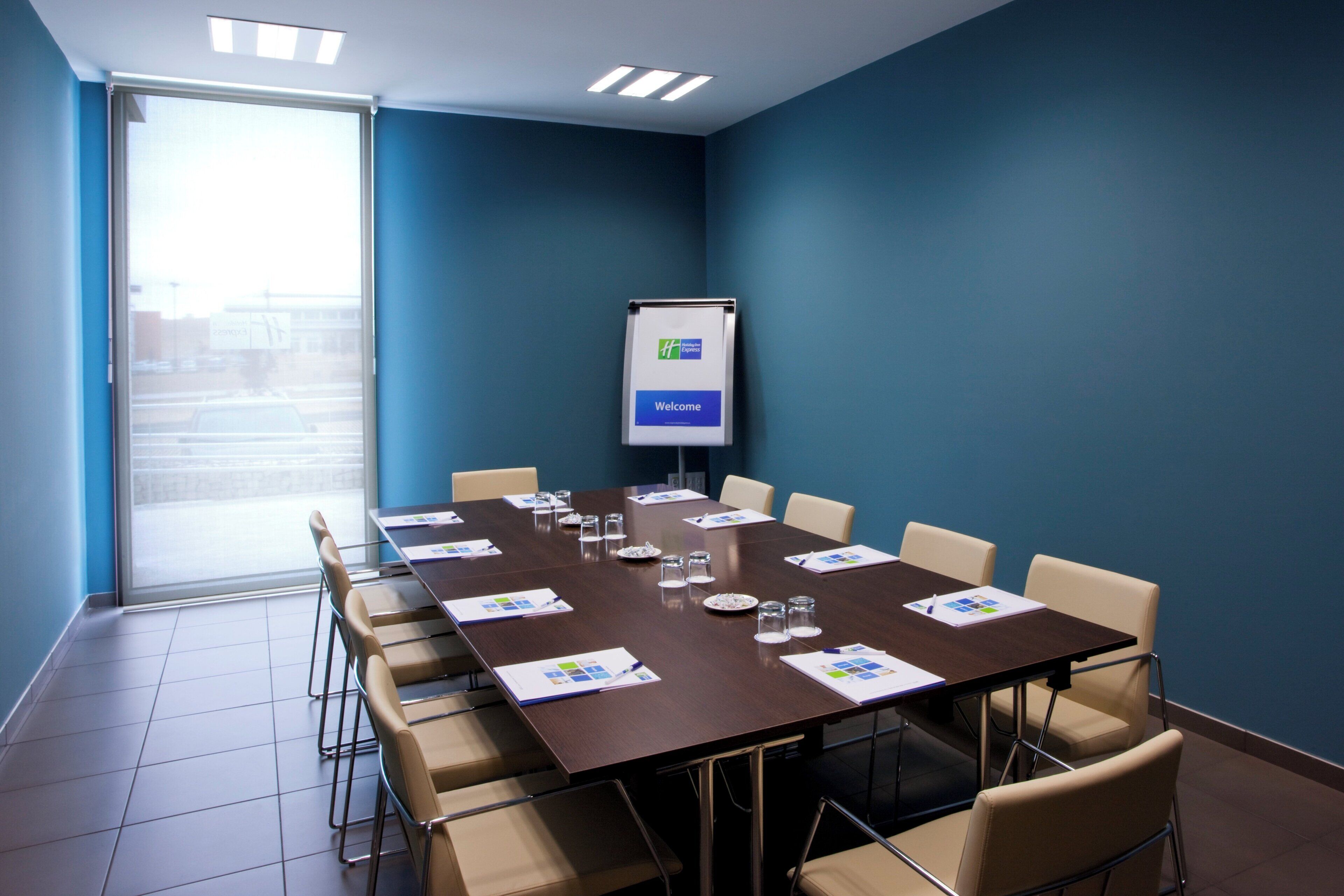 Sala de conferência com mesa comprida, cadeiras, quadro branco e porta de vidro que dá para o exterior.