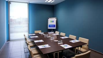 Sala de conferência com mesa comprida, cadeiras, quadro branco e porta de vidro que dá para o exterior.