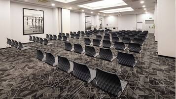 Uma sala de conferências com fileiras de cadeiras, um projetor e um quadro branco.