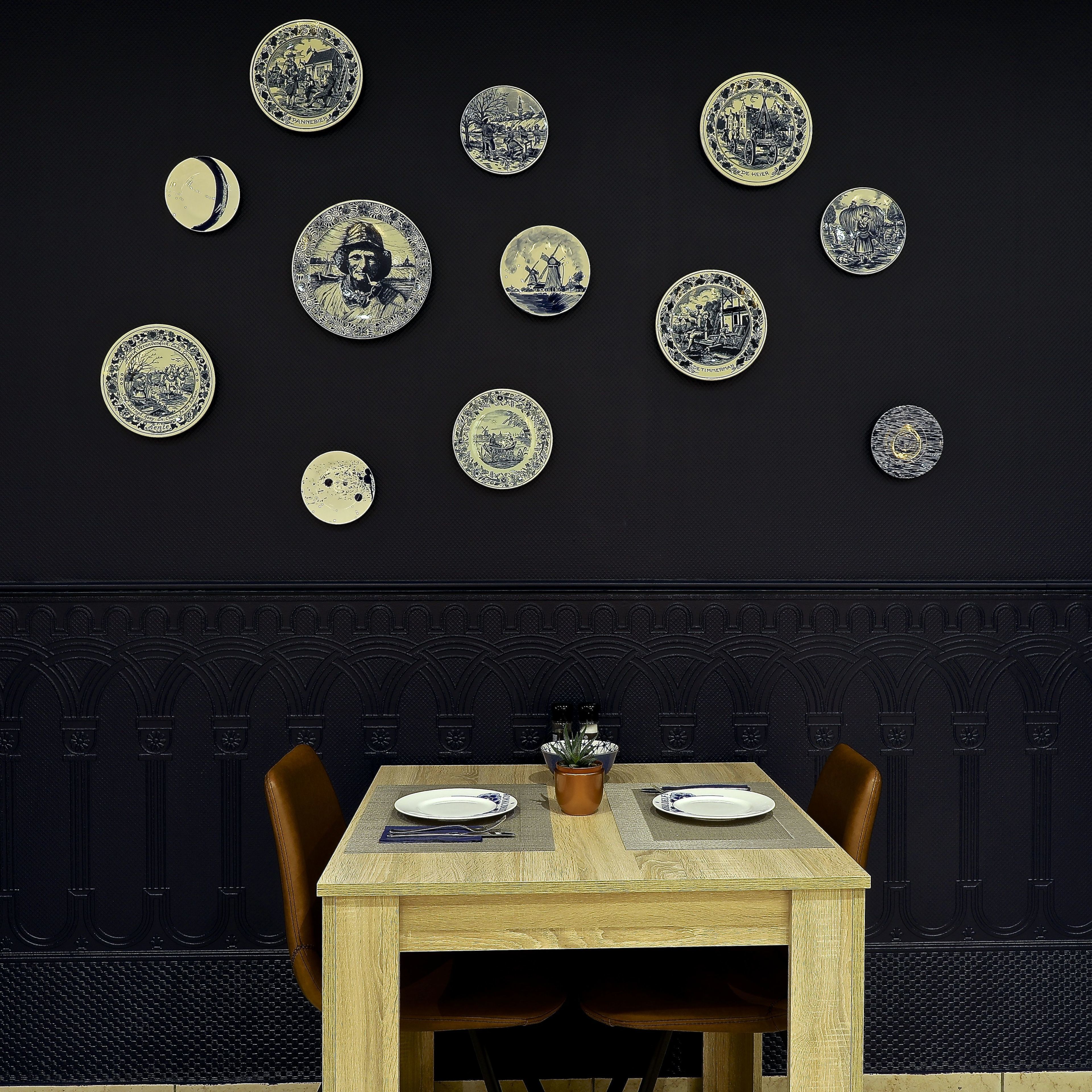 Uma sala de jantar com uma mesa posta para dois, destacando uma parede escura com pratos decorativos e uma parede inferior com textura.