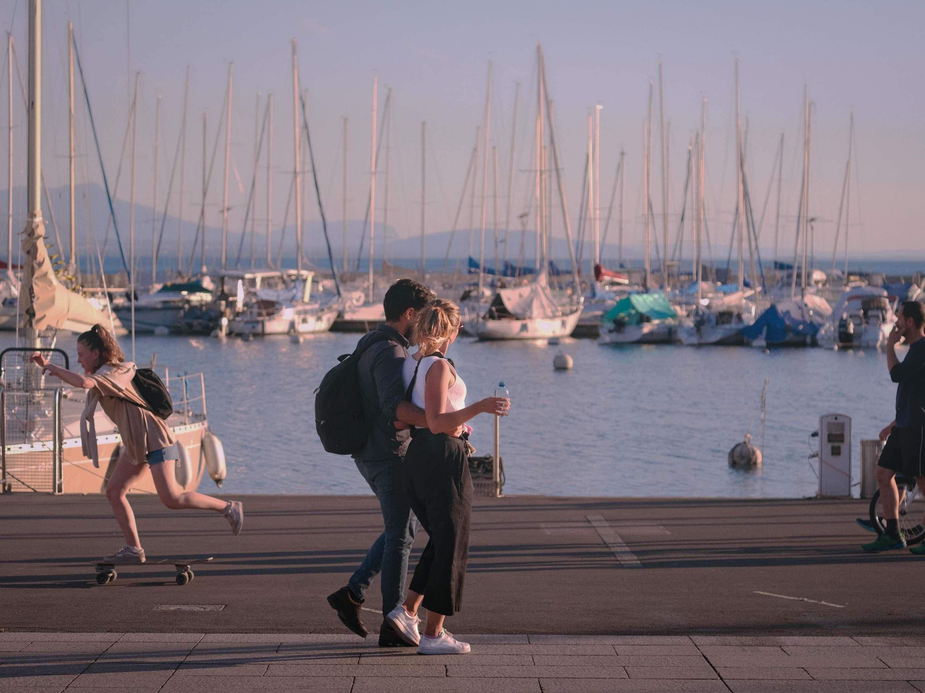 Uma marina com barcos e um casal passando.
