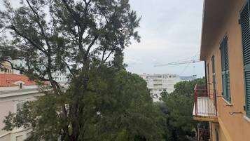 Edifício residencial com varanda, uma grande árvore em primeiro plano e vista ampla do bairro ao redor.