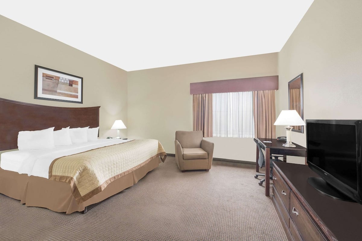 Quarto de hotel com uma cama, uma cadeira, uma escrivaninha com televisão e uma janela com cortinas.