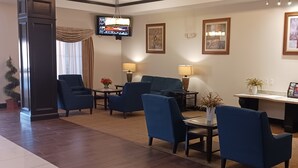 Um saguão de hotel com área de estar, uma televisão fixada na parede e um balcão de recepção.