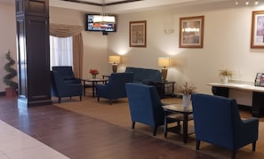Um saguão de hotel com área de estar, uma televisão fixada na parede e um balcão de recepção.