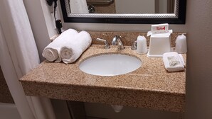 Uma pia de banheiro com bancada de granito, um espelho e artigos de higiene pessoal, incluindo toalha, sabonete e tônico facial.