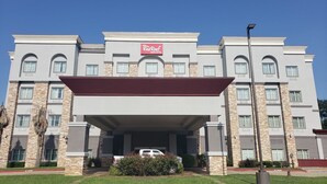 Edifício Red Roof Inn & Suites com design arquitetônico moderno, apresentando entrada central com toldo vermelho, fachada de pedra e várias janelas.