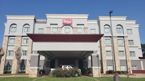 Edifício Red Roof Inn & Suites com design arquitetônico moderno, apresentando entrada central com toldo vermelho, fachada de pedra e várias janelas.