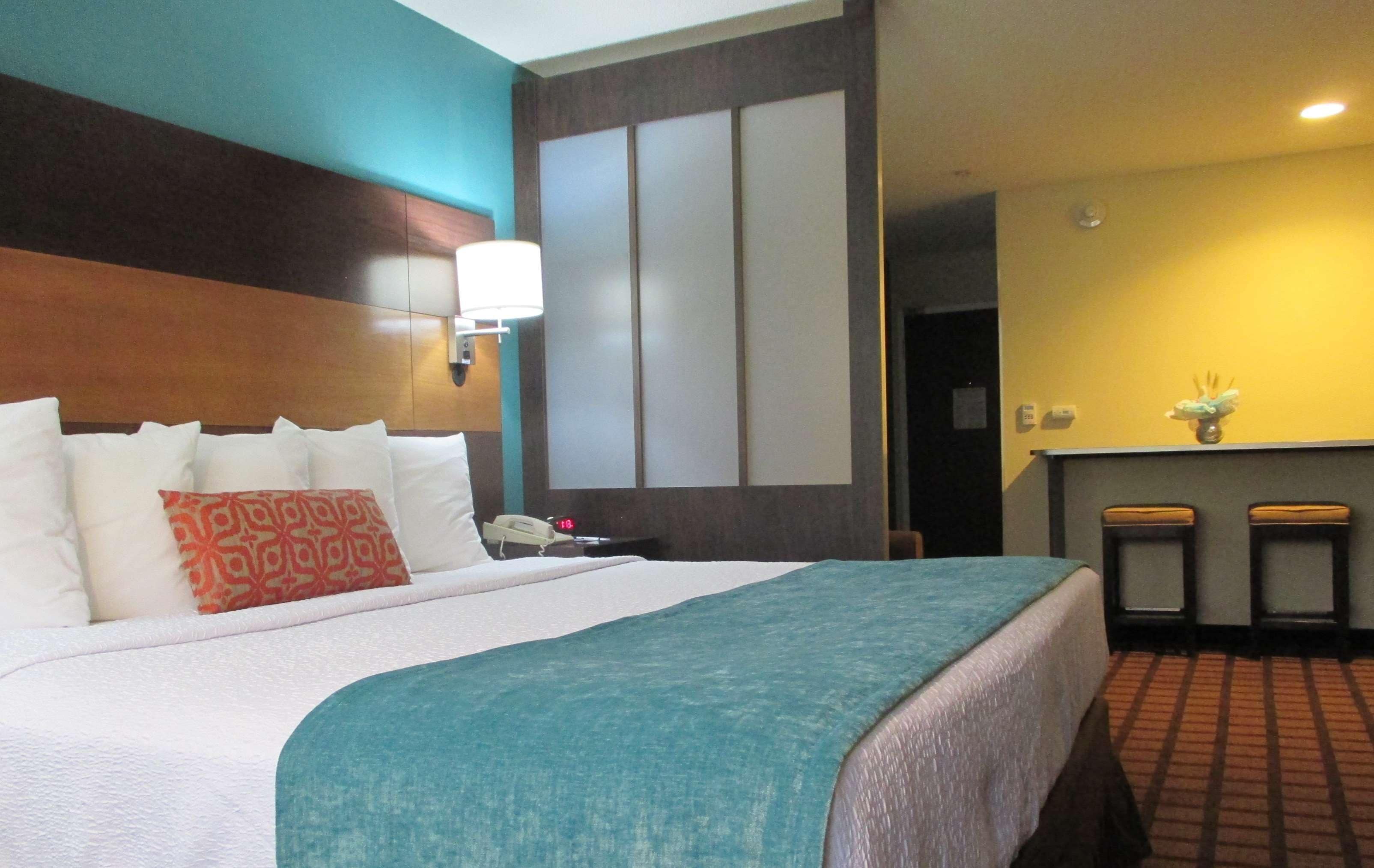 Quarto de hotel com uma cama grande, um abajur, um telefone e dois banquinhos.