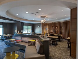 Um lobby de hotel moderno com teto curvo, área de estar central com sofás e mesas, e divisória de madeira com vista para o exterior.